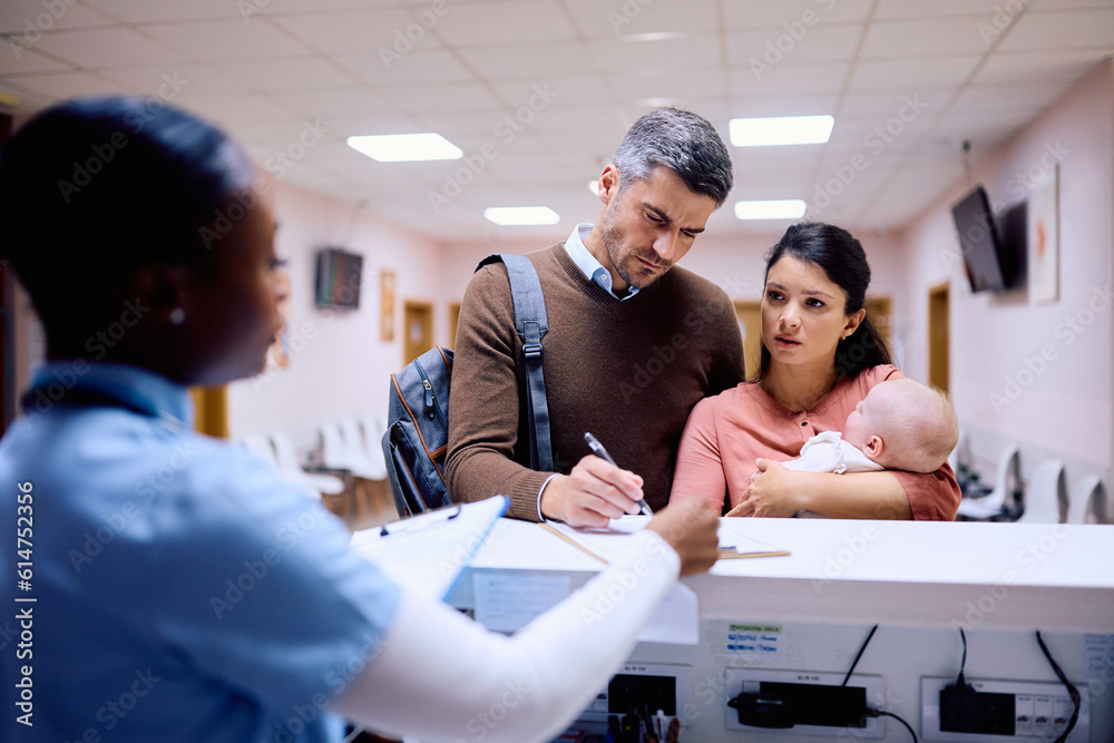 Parents with baby registering at reception desk at doctor's office ...
