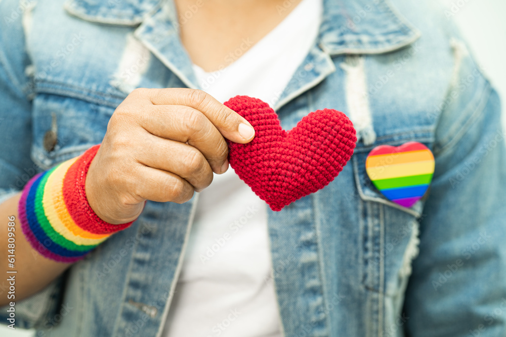 Asian lady wearing rainbow flag wristbands and hold red heart, symbol ...