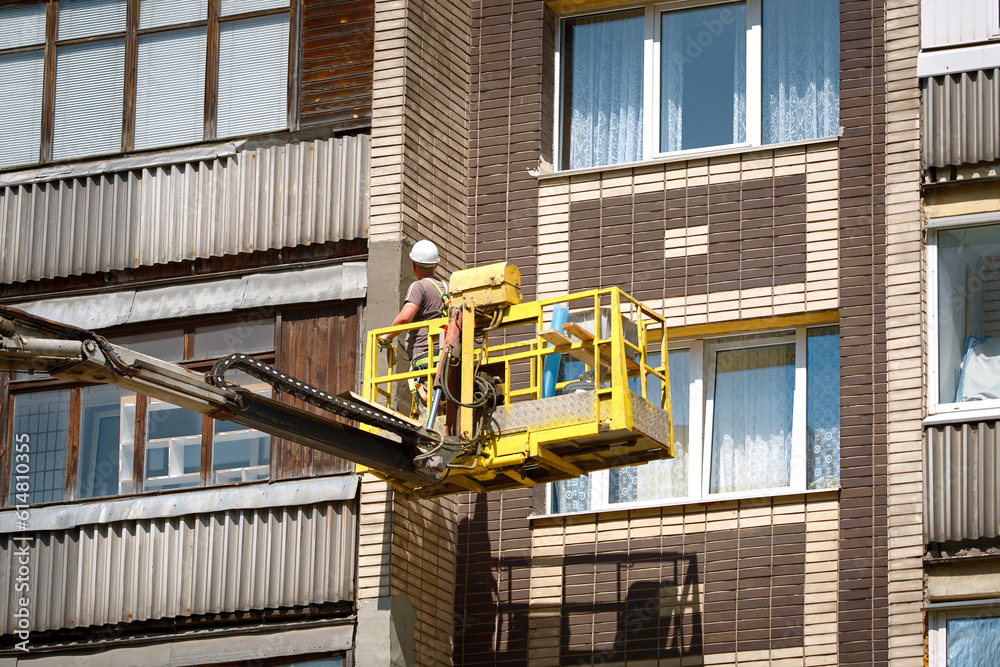 Man on aerial platform plastering wall of residential building ...