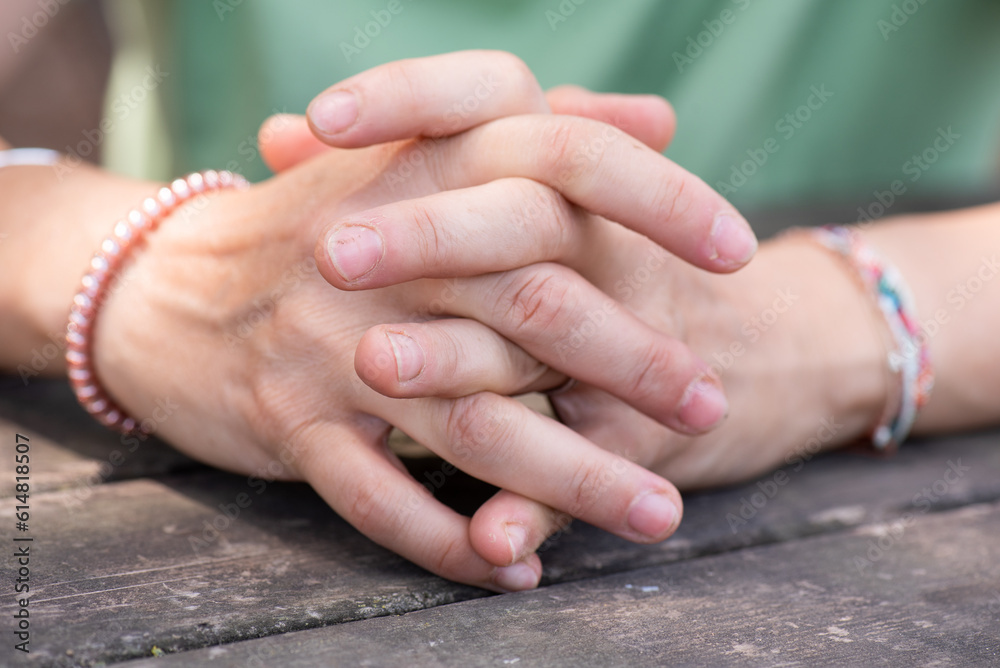 detail of crossed hands of woman in her forties with thin bracelets out ...