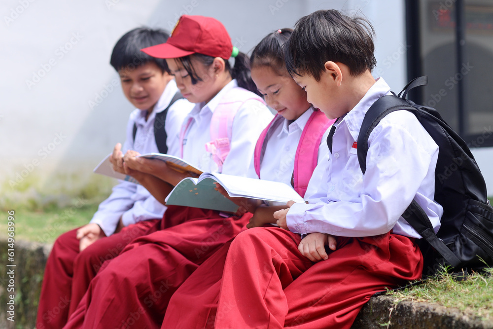 School kids in uniform sitting in a row and reading book together ...
