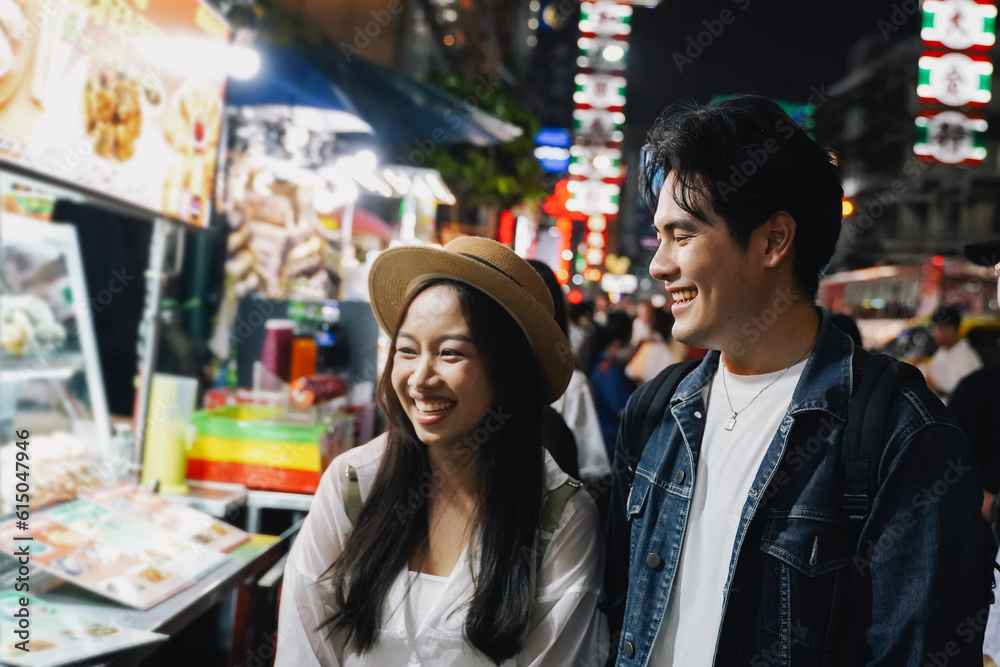 Asian couple tourist backpacker enjoying and eating street food in night market with crowd of ...