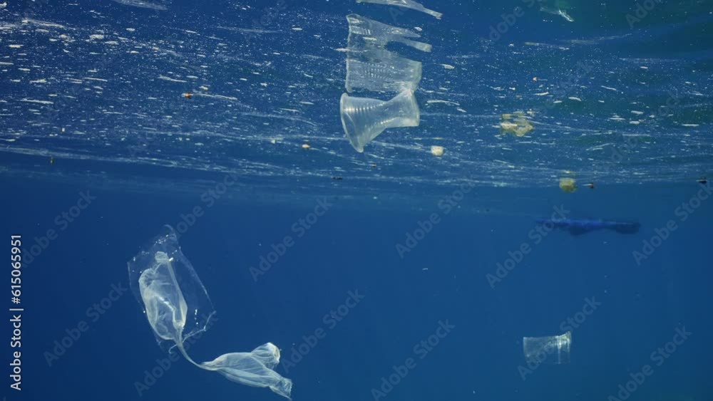 Plastic trash floats in blue Ocean of polluted water reflecting on its ...