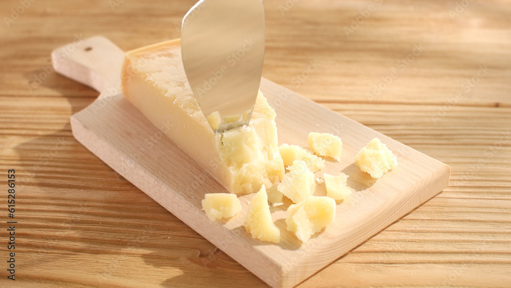 Hard cheese is chipped off with a knife on a cutting board. Wooden ...