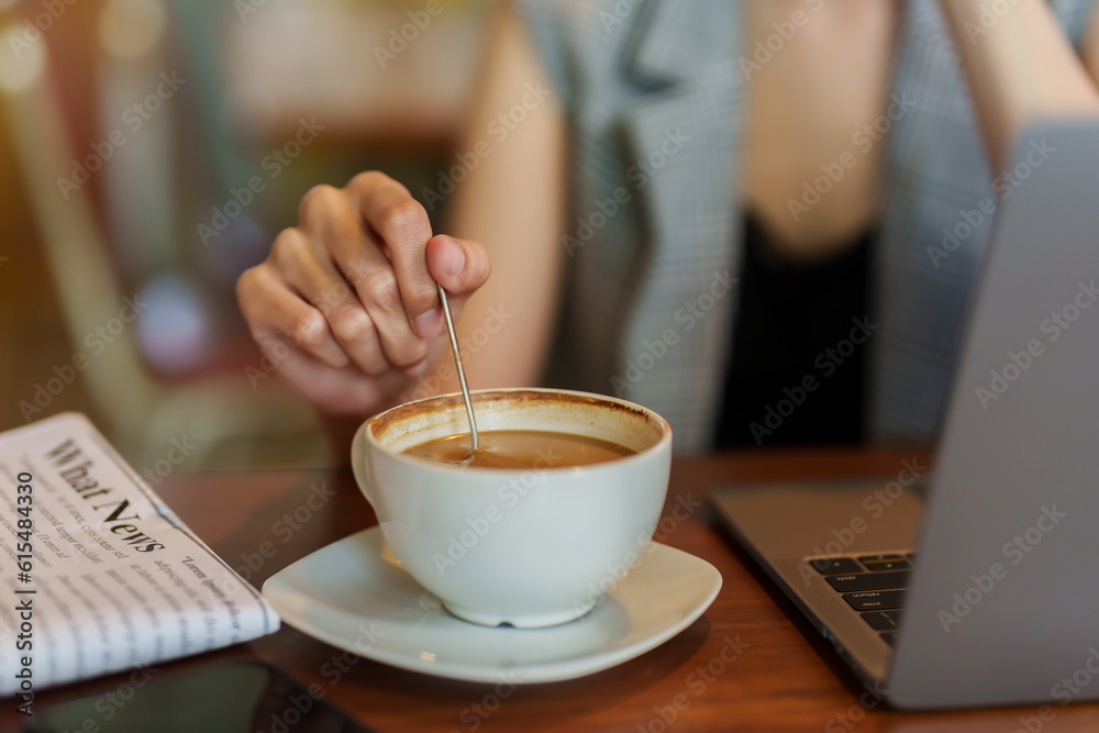 Close-up shot of coffee cup lying on table with woman's hand. Use a spoon to stir the coffee cup ...