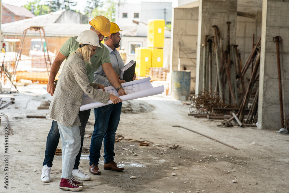 A female architect and construction manager work together on-site, discussing blueprints and ...