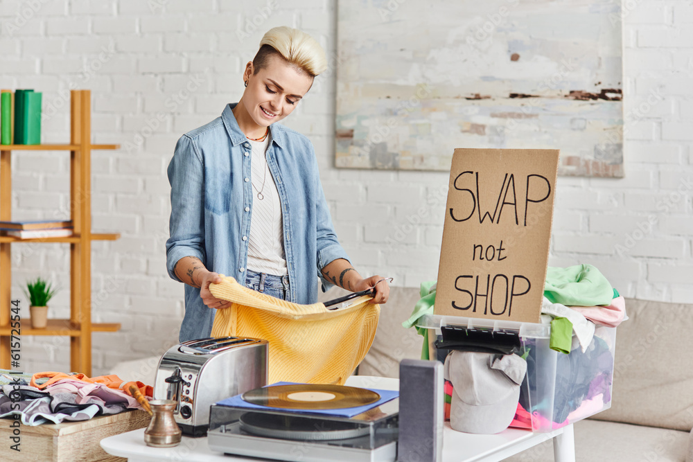 happy tattooed woman looking at yellow jumper near vinyl record player ...