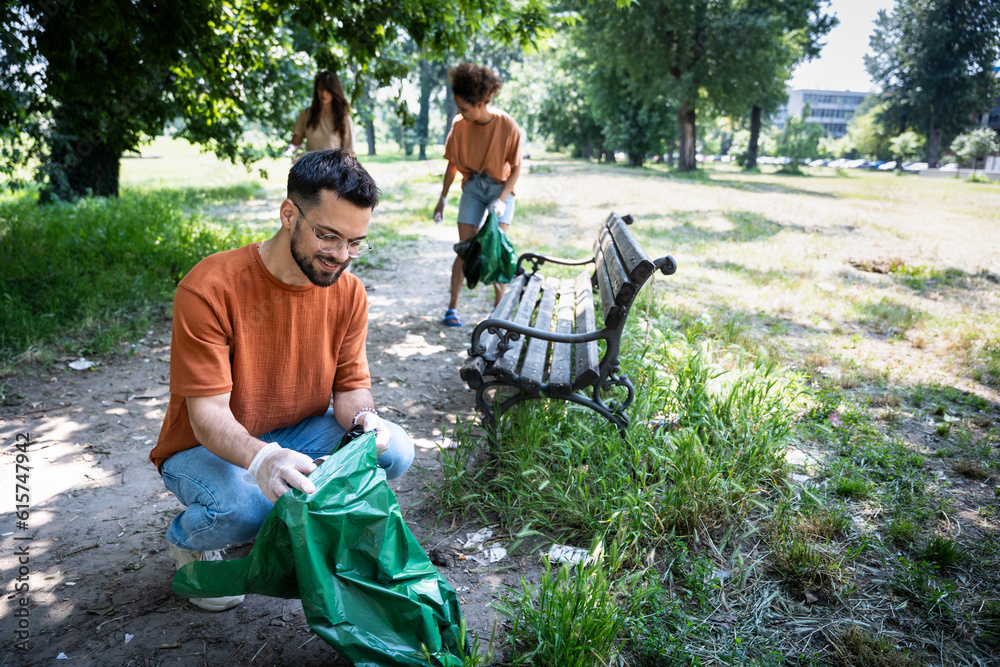 Foto de Young volunteers cleaning up park together, collecting trash ...