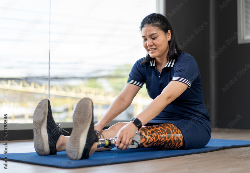 Prosthetic leg woman sitting on mat doing physical exercise in fitness ...