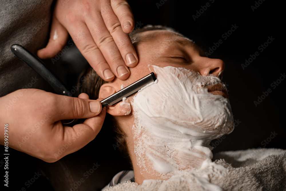 Barber man shaving young attractive client with vintage straight razor ...