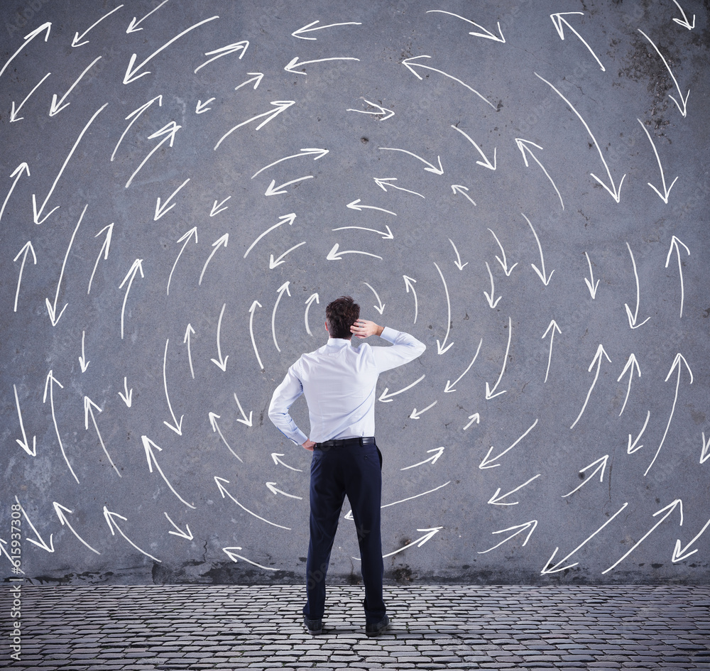Foto de Confused businessman looking a wall with directional arrows ...