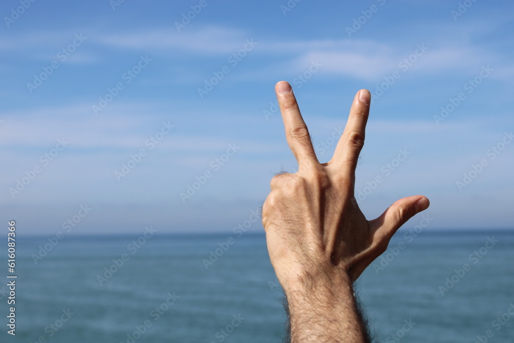 Hand doing,showing number three gesture symbol on blue summer sky ...