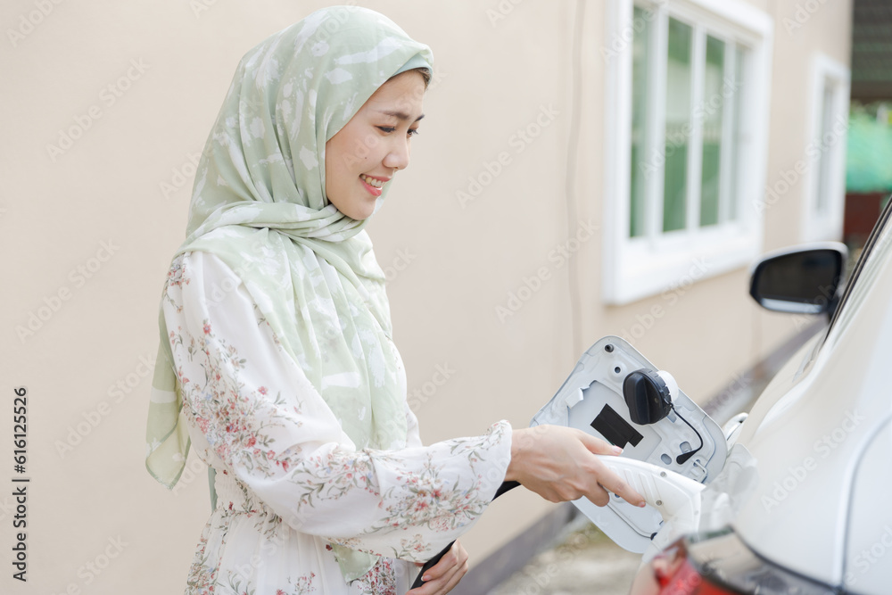 Muslim Islamic women using a charging pump into an EV car electric ...