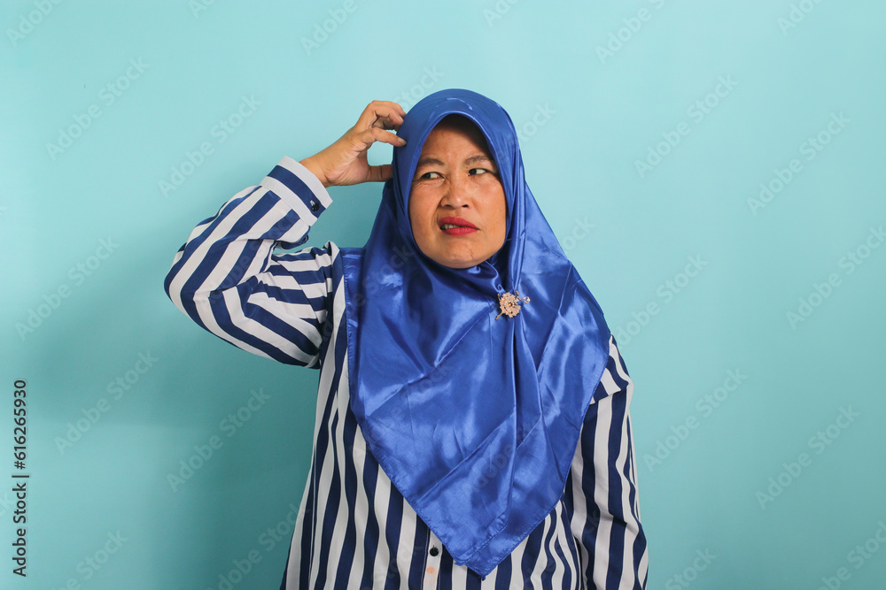 A confused middle-aged Asian woman in a blue hijab and striped shirt ...
