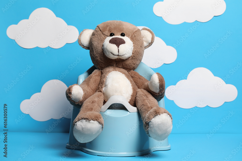 Teddy bear on baby potty against light blue background with paper ...