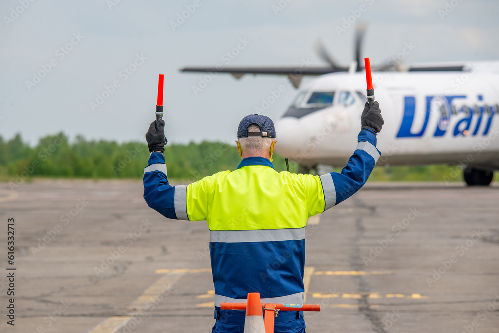 Rear view A signalman meets a passenger plane at the airport in front ...