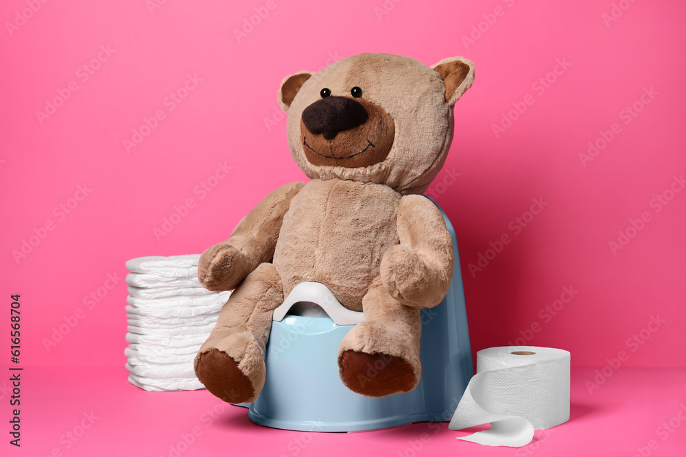 Teddy bear on baby potty, toilet paper and stack of diapers on pink ...