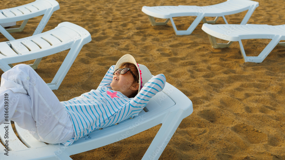 beautiful little girl resting on a sun lounger next to the pool against ...