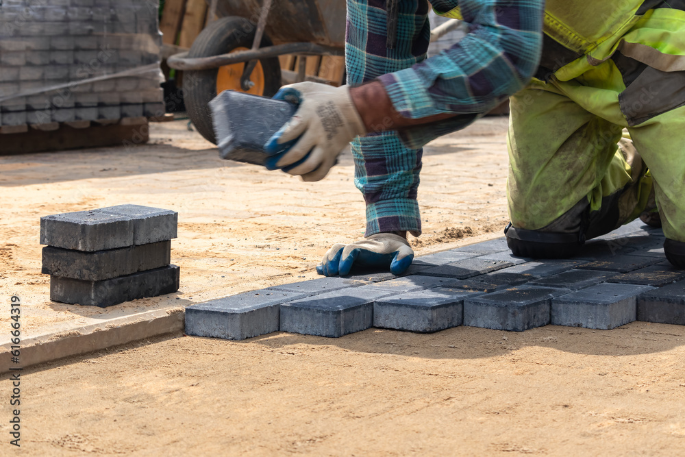 A worker laying paving stones at a sidewalk construction site, close up ...