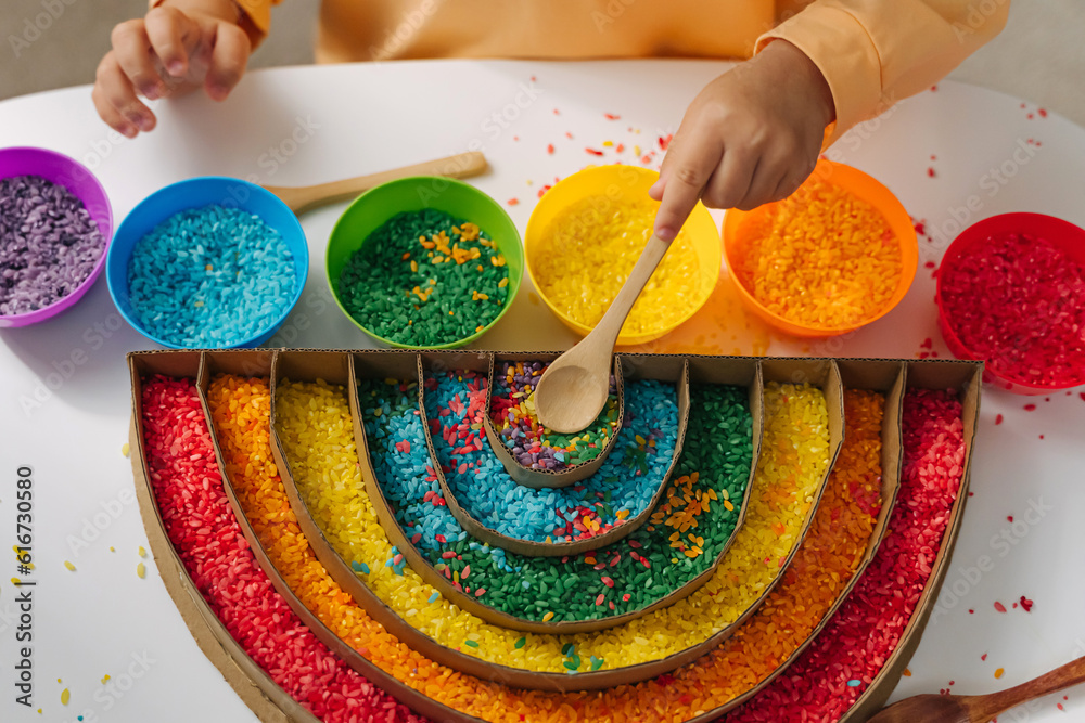 Child hands playing colored rice and make rainbow. Child filled the ...