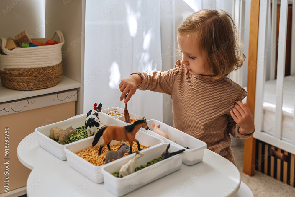 A little girl playing with farm animals in sensory bin in nursery ...