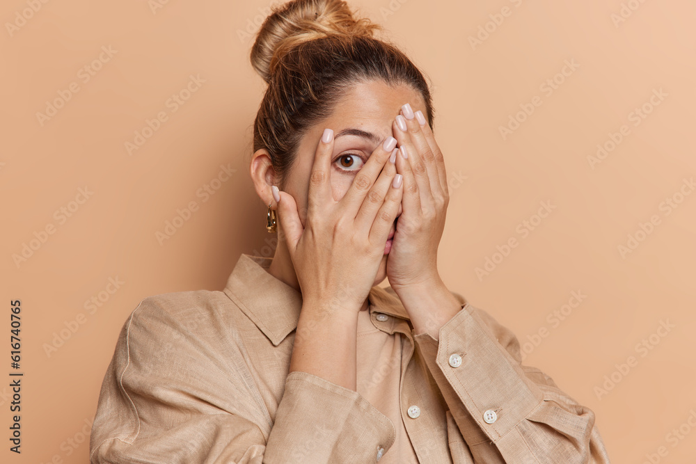 Young European woman delicately peeks through trembling fingers her ...