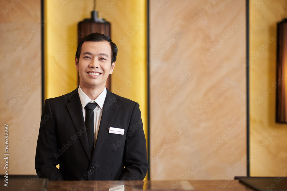 Portrait of positive Asian hotel receptionist with badge on his suit ...