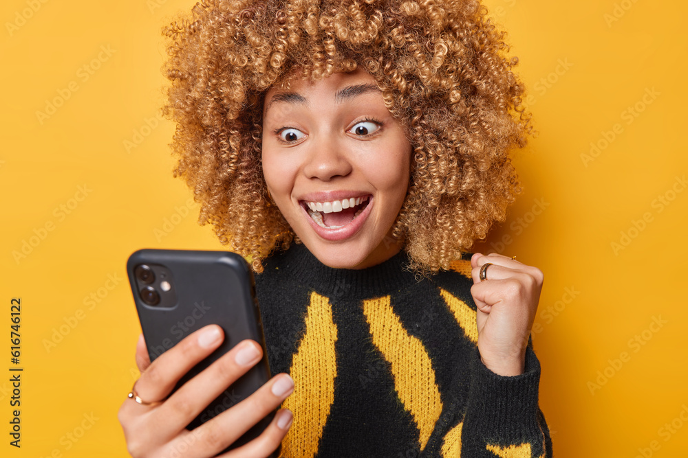 Positive surprise curly haired young woman celebrates moment of triumph ...