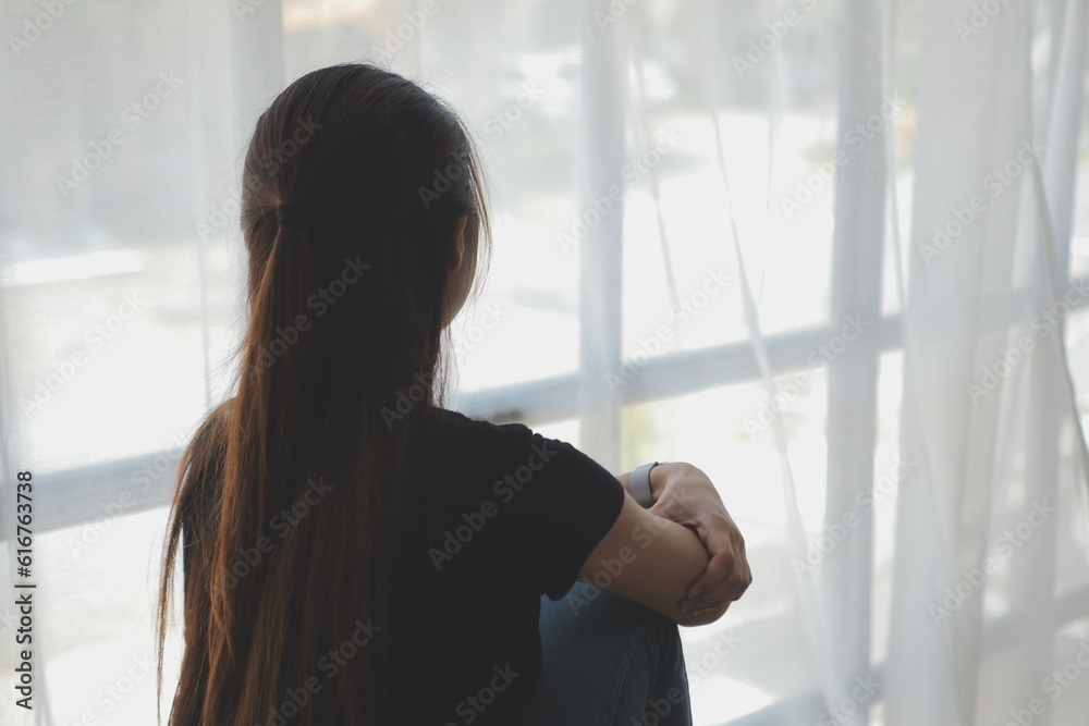 Thoughtful girl sitting on sill embracing knees looking at window, sad ...