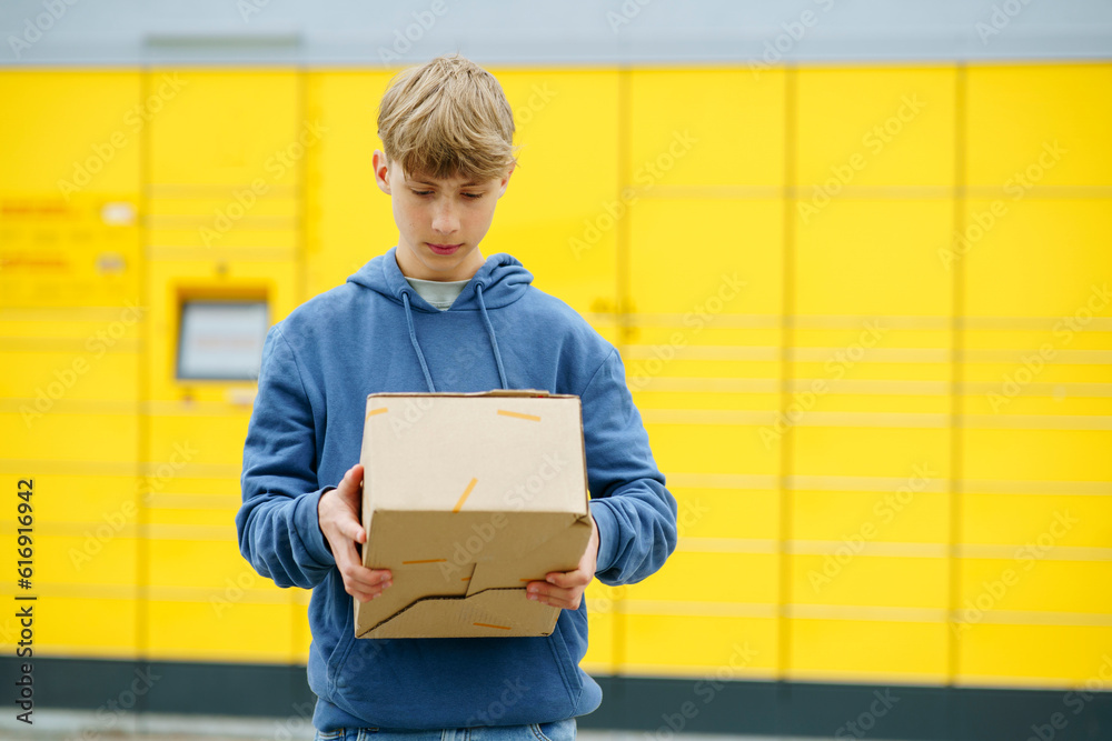 Boy examining package standing in front of yellow parcel locker Stock ...