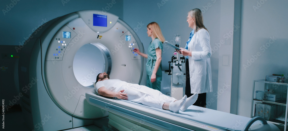 Young man lies down in MRI capsule. Chief head doctor in dressing gown ...