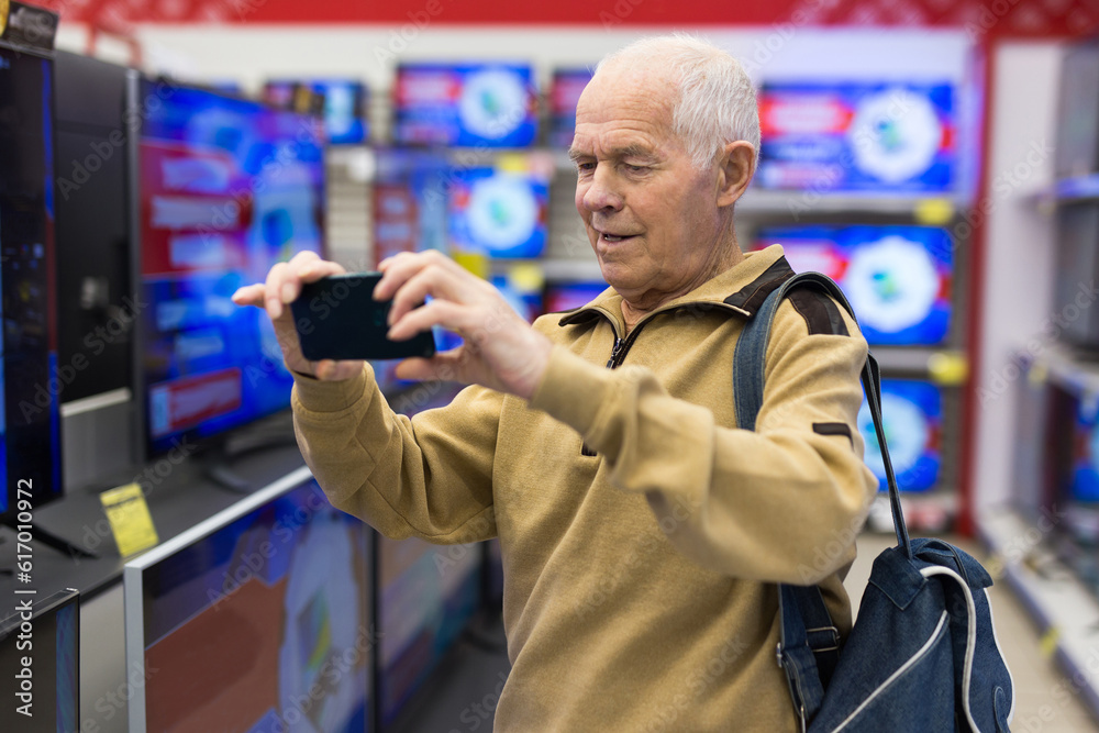 senor man pensioner scanning QR code modern digital televisor with smart tv in showroom of ...