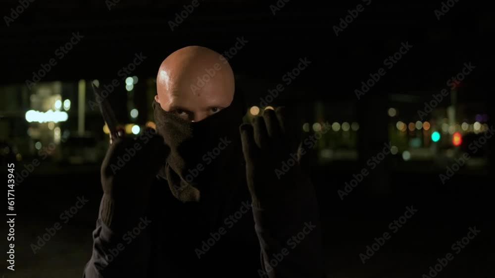 An evil criminal in a black mask takes out a knife and starts waving it ...