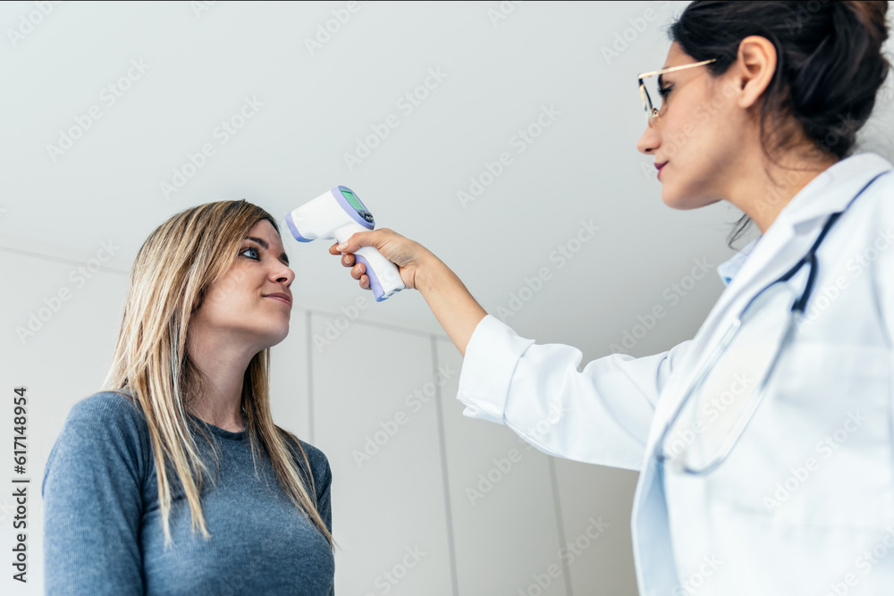 Cheerful beautiful female doctor taking woman patient temperature with ...