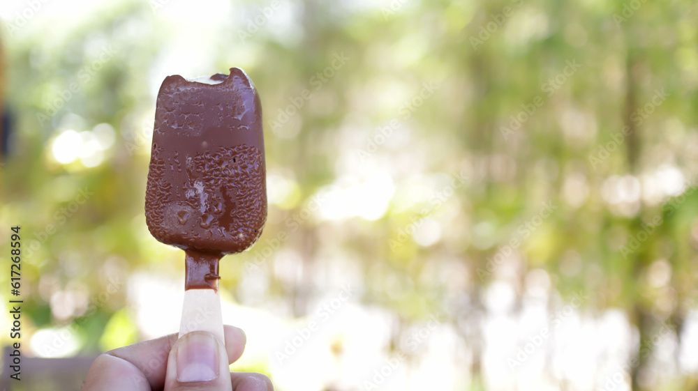 A hand holding bitten common popular dark chocolate ice cream stick or ...
