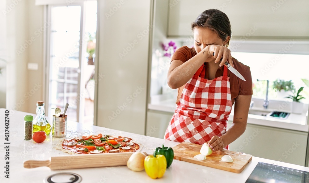 Young beautiful hispanic woman cutting onion crying at the kitchen Stock Photo | Adobe Stock