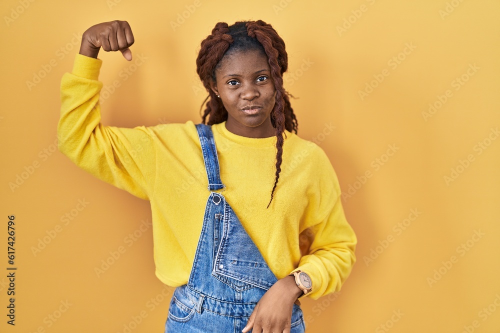 African woman standing over yellow background strong person showing arm ...