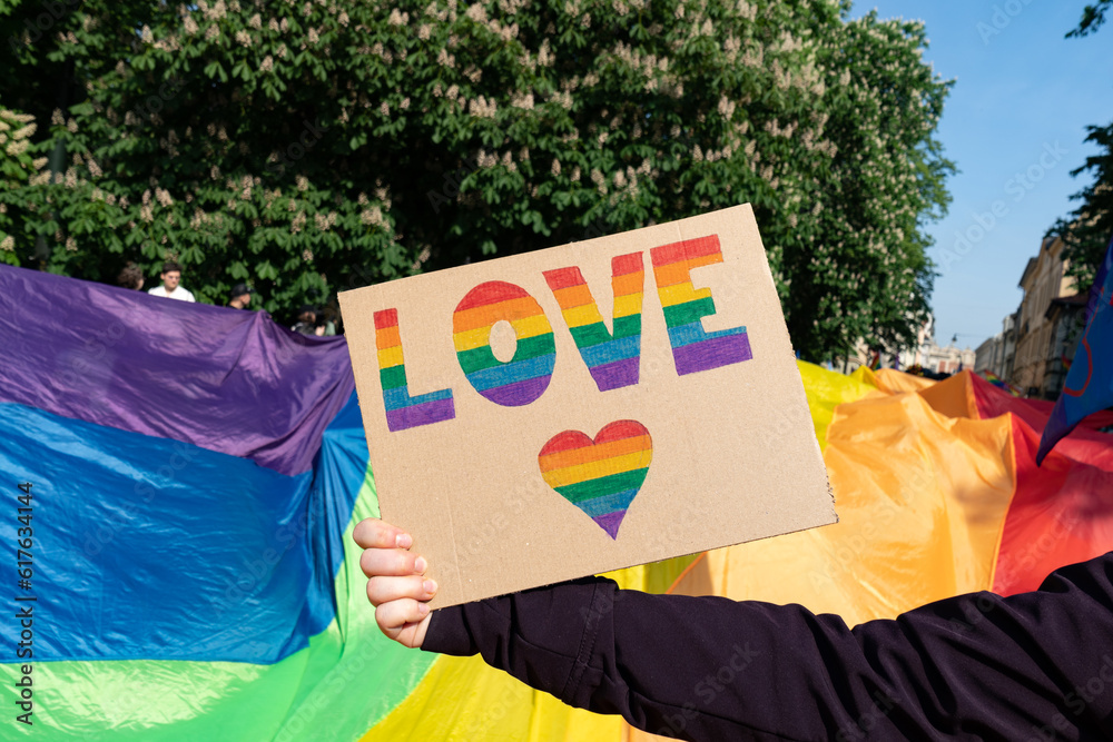 Hand holding placard sign with text Love and rainbow flag heart, during ...