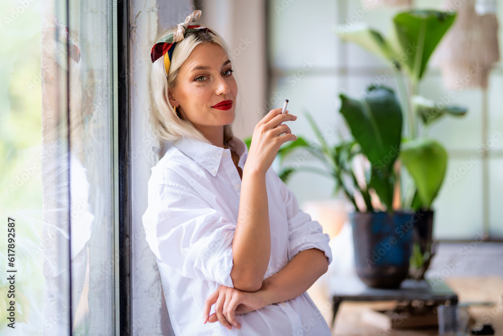 Beautiful blond haired woman with hair scarf standing at the window and ...