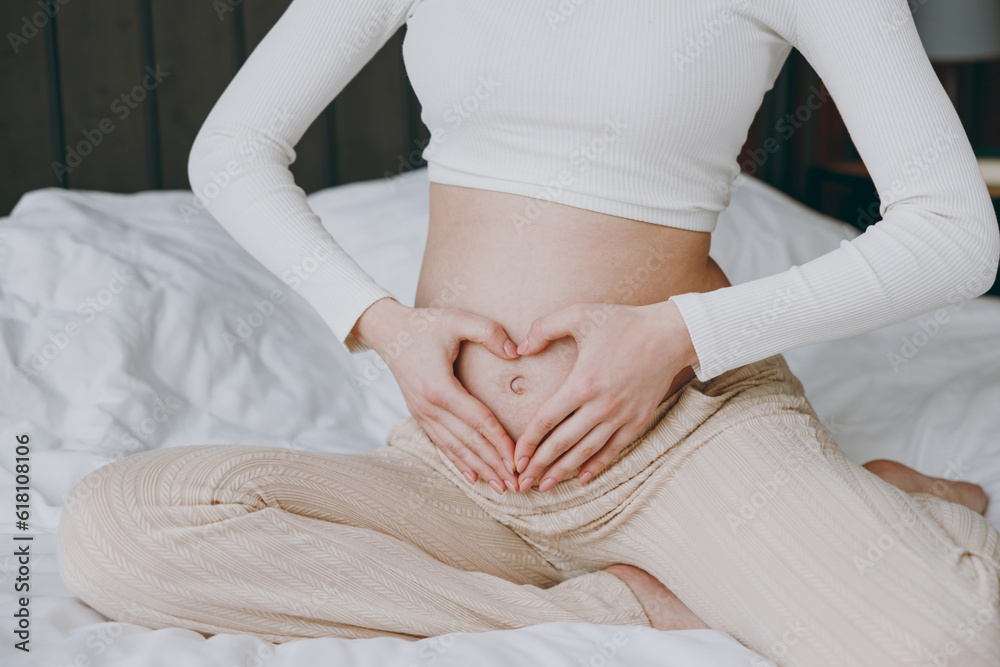 Cropped close up young pregnant woman wear white pyjamas hold hnds in ...