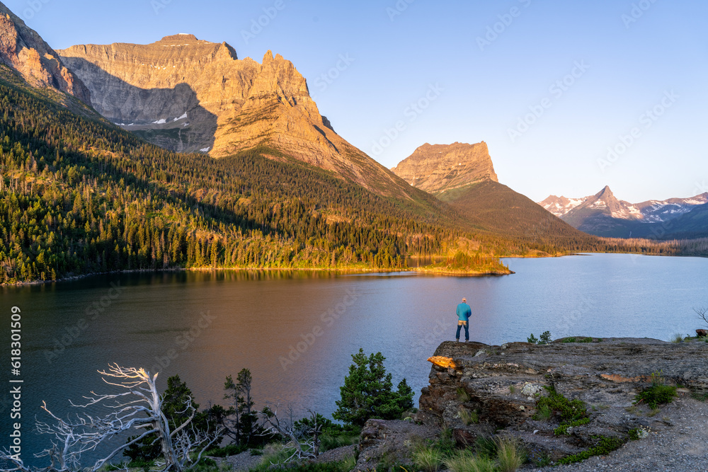 Man standing on a rock cliff looking at a scene of a lake and rugged ...
