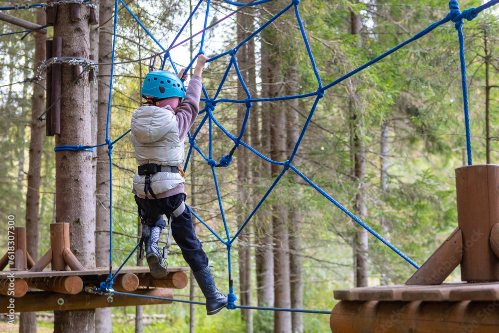 A child wearing a helmet and safety ropes will pass rope trails in a ...