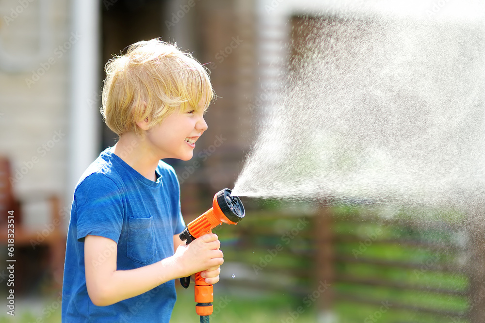 Funny little boy watering lawn and playing with garden hose with ...