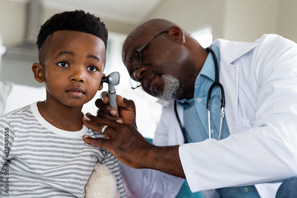 Senior african american male doctor checking ear of boy patient with ...