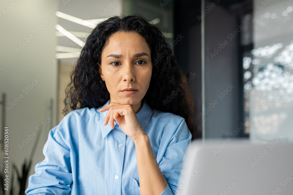 Serious thinking woman working inside office at workplace with laptop ...
