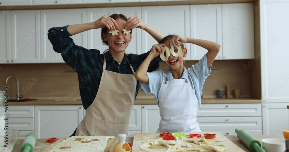 Overjoyed mother and little daughter in aprons making funny faces ...