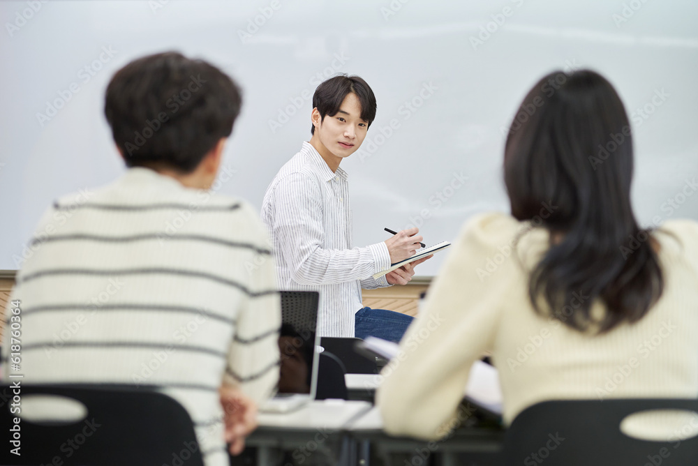 An Asian young man is standing in front of a lecture hall at a ...