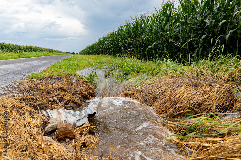 Storm water flowing in ditch between road and farm field. Agriculture ...