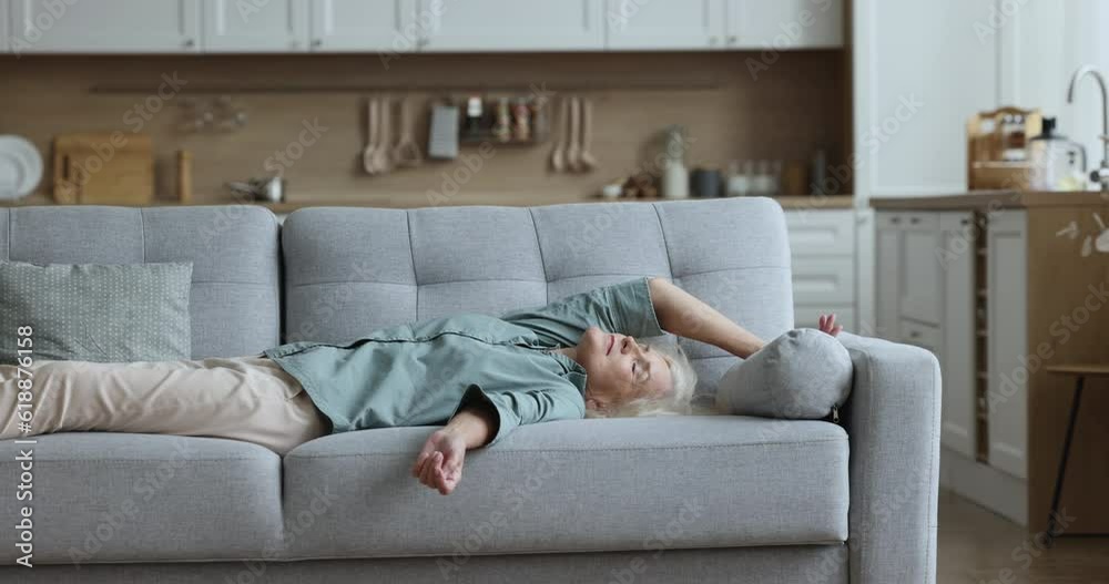 Exhausted senior older blonde woman falling down on soft couch, lying ...