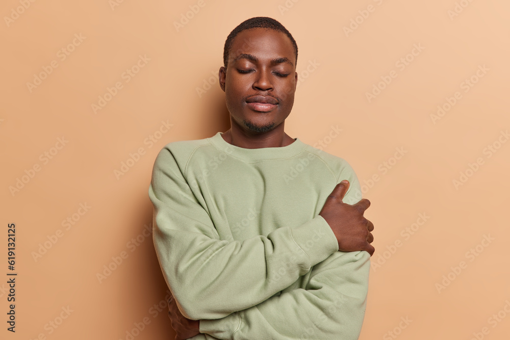 Calm dark skinned man lovingly embraces himself embodying essence of ...